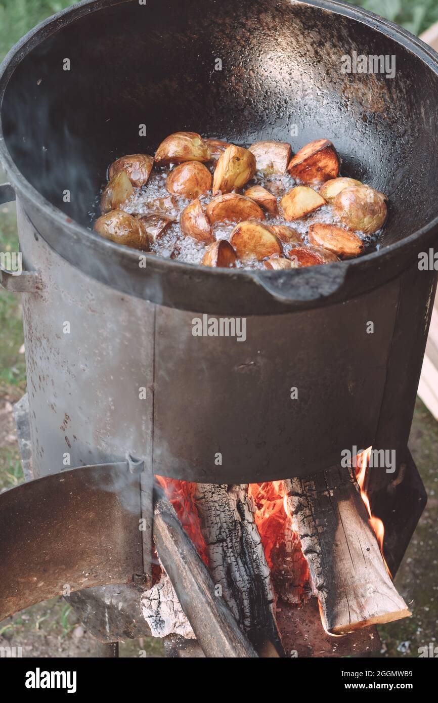 Baked potatoes cooked in yard cauldron with firewood burning in it with ...