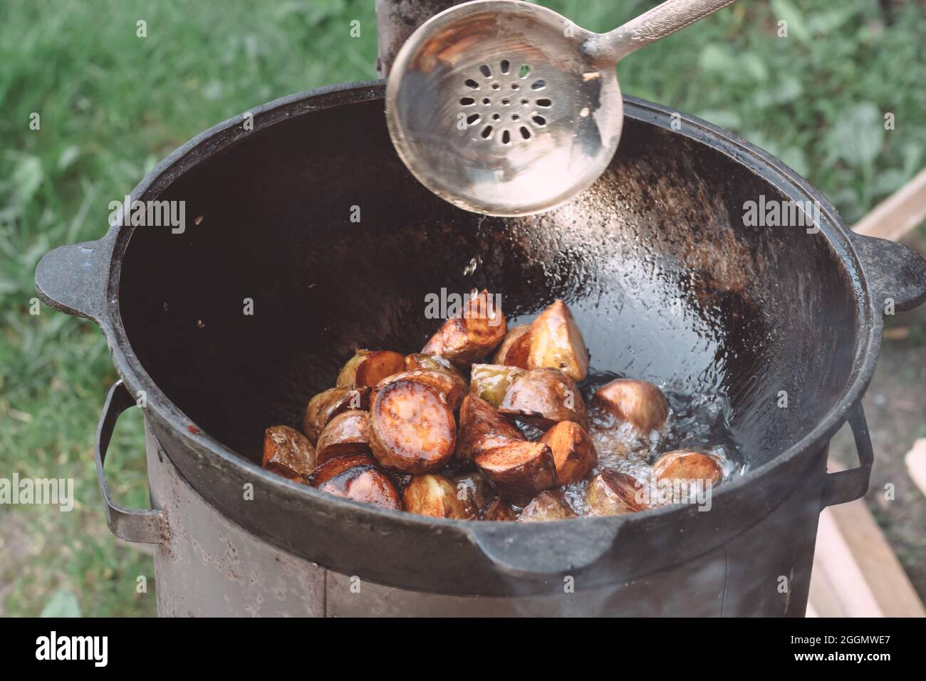 Baked potatoes cooked in yard cauldron with firewood burning in it with ...