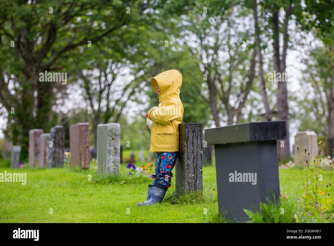 Sad little child, blond boy, standing in the rain on cemetery, sad ...
