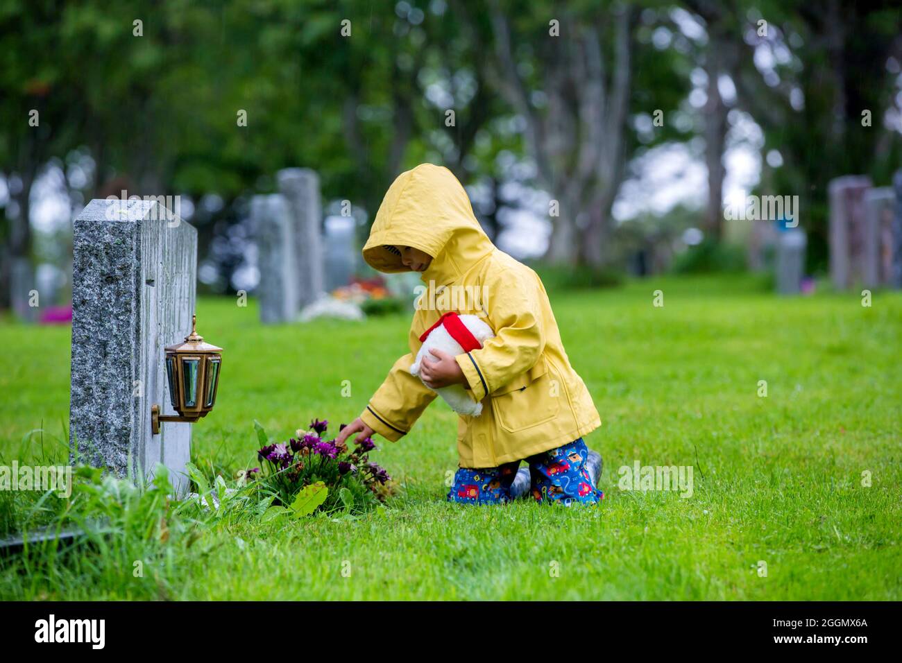 Sad little child, blond boy, standing in the rain on cemetery, sad ...