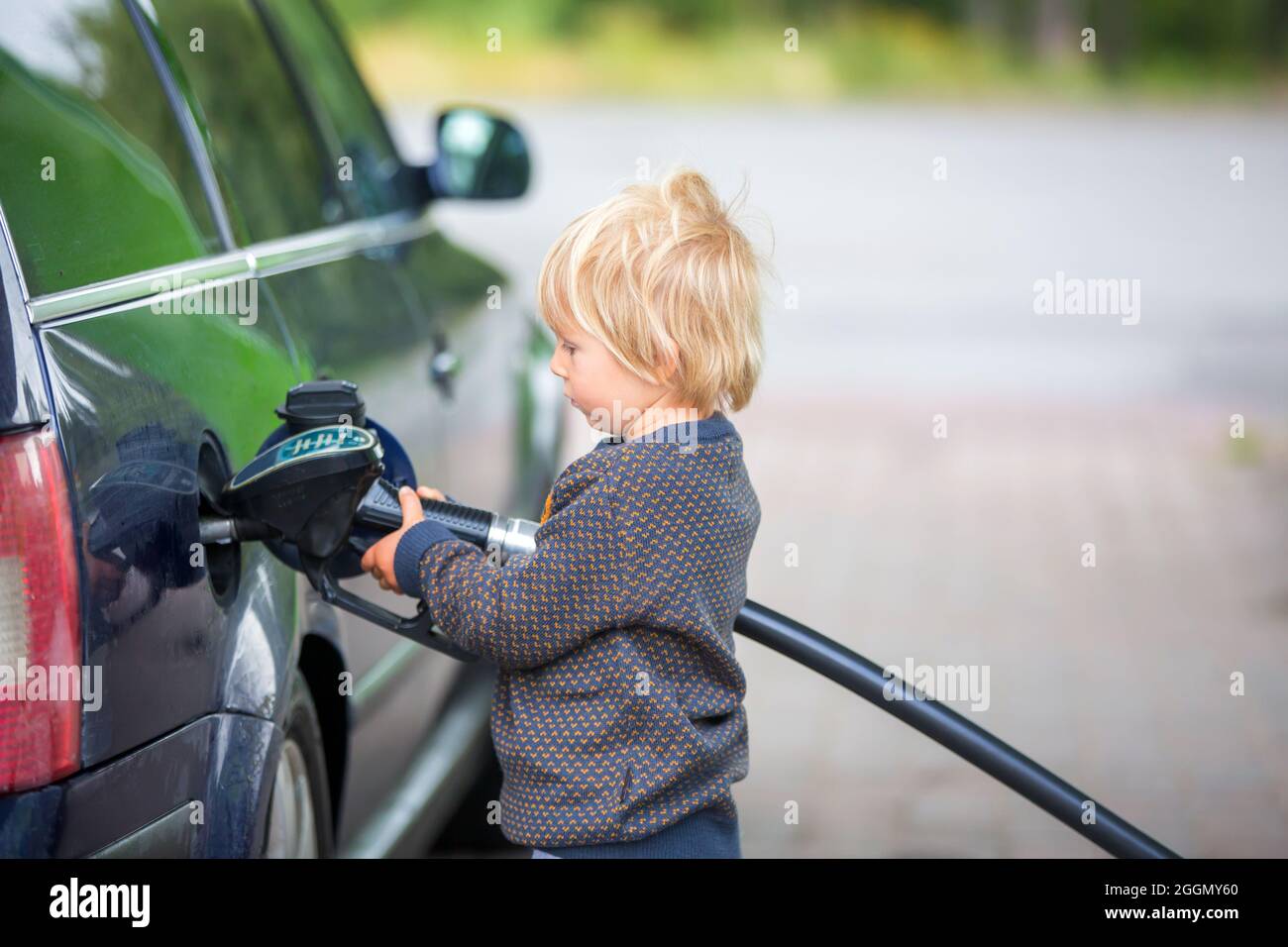 Sweet little child, blond boy, helping parents to put fuel in the car ...