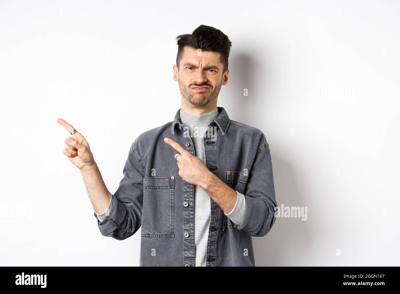 Skeptical and disappointed young man pointing fingers left, grimacing ...