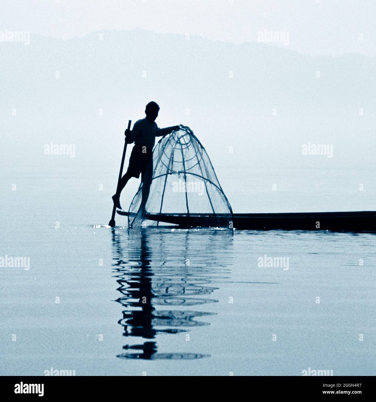 Bygone lifestyle: a leg rower fisherman stands on the back of a boat ...