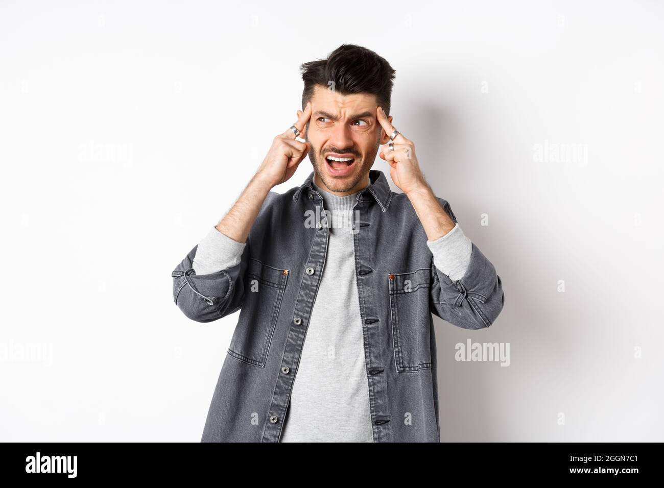 Distressed young man touching head and shouting, looking frustrated ...