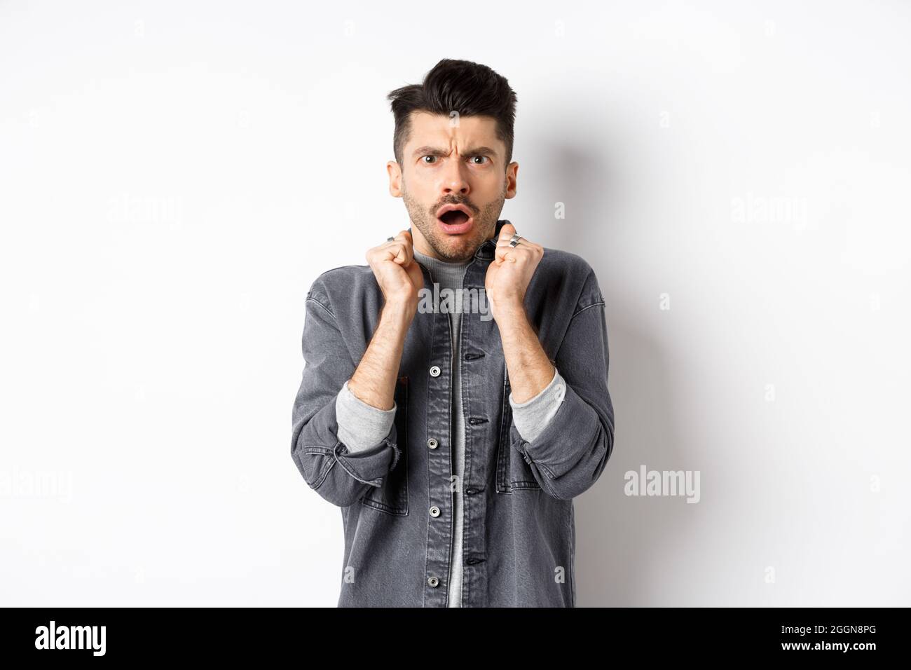 Shocked young man look confused and offended, gasping and frowning at ...