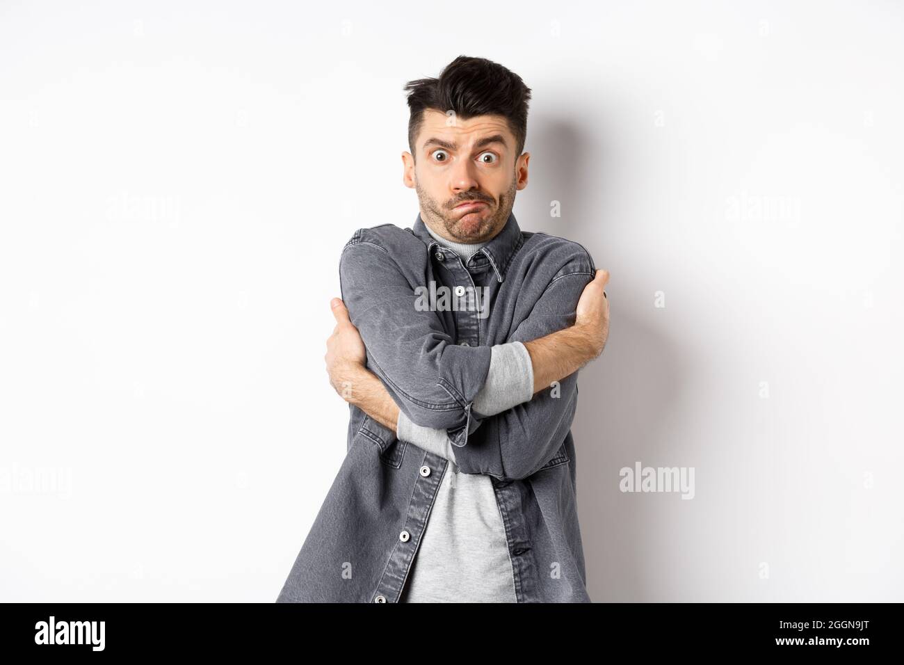 Funny young man hugging himself and grimacing, feeling embarrassed and ...