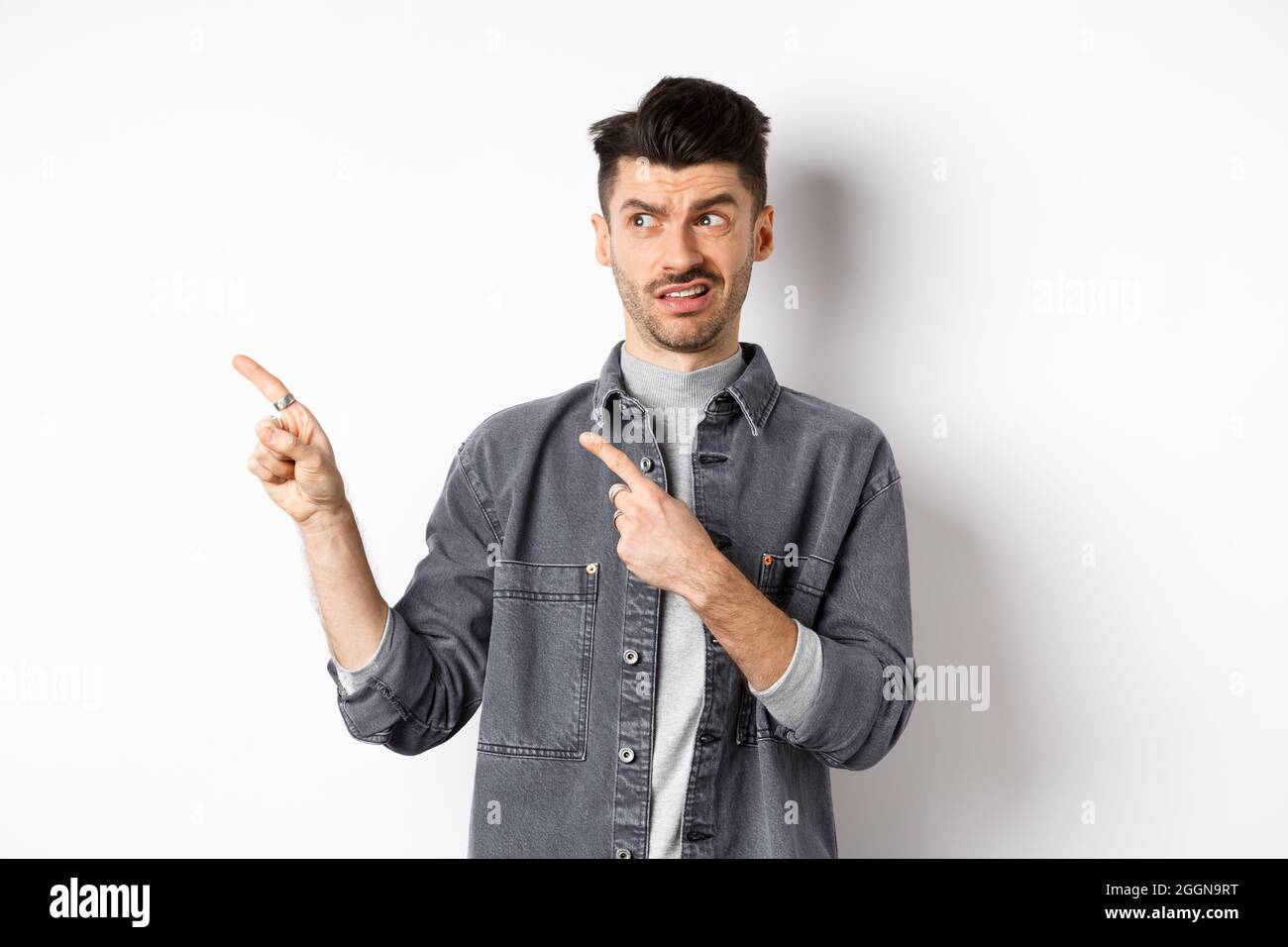 Skeptical and doubtful young man pointing fingers left at logo, look ...