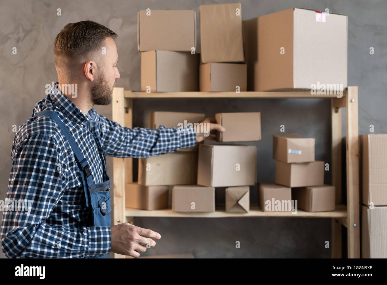 Caucasian male worker dressed in blue overalls stands near a shelf with ...