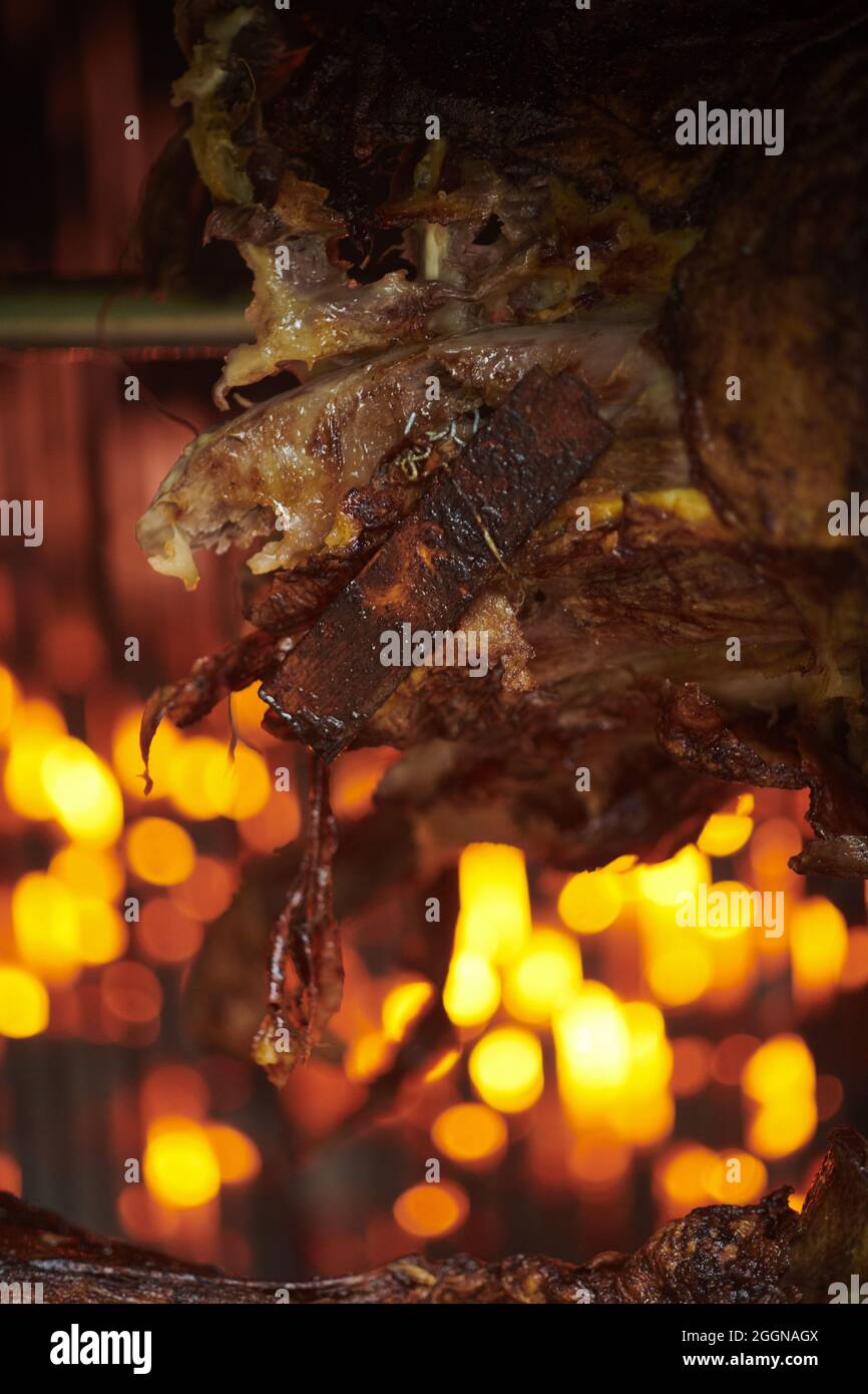 Closeup shot of roasting pork on a spit with fire in the background ...