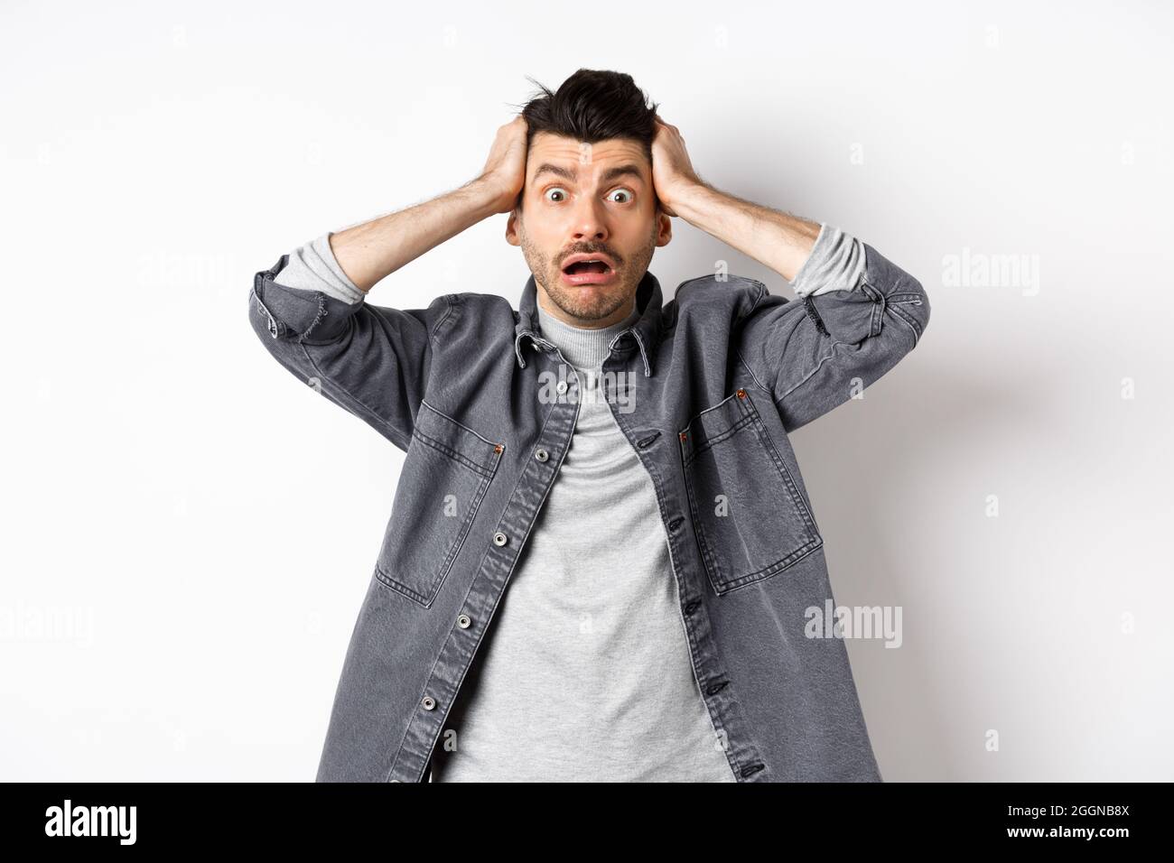 Alarmed young man grab head and pop eyes at camera, looking worried and ...
