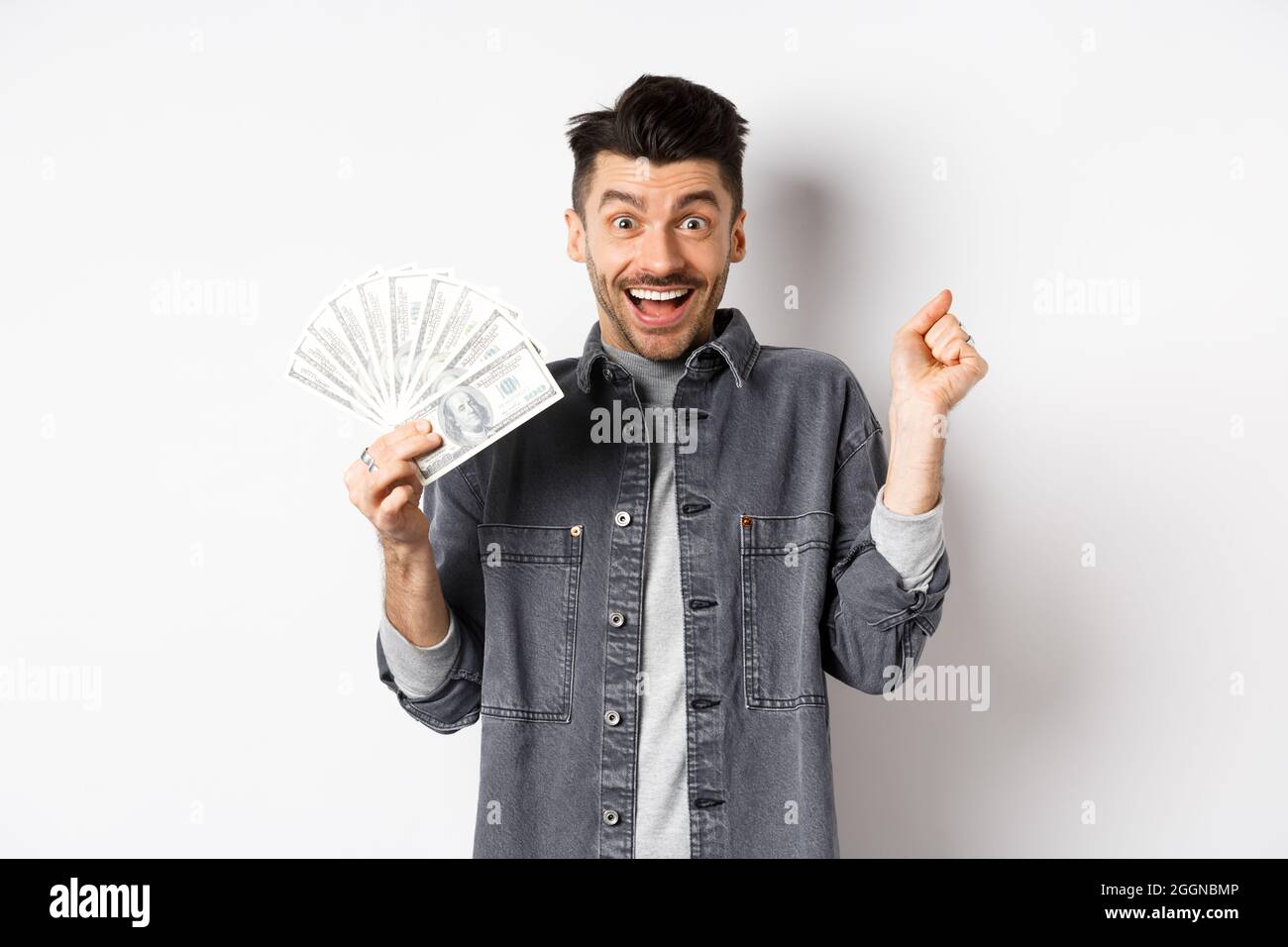 Cheerful young man jumping from excitement and showing dollar bills ...