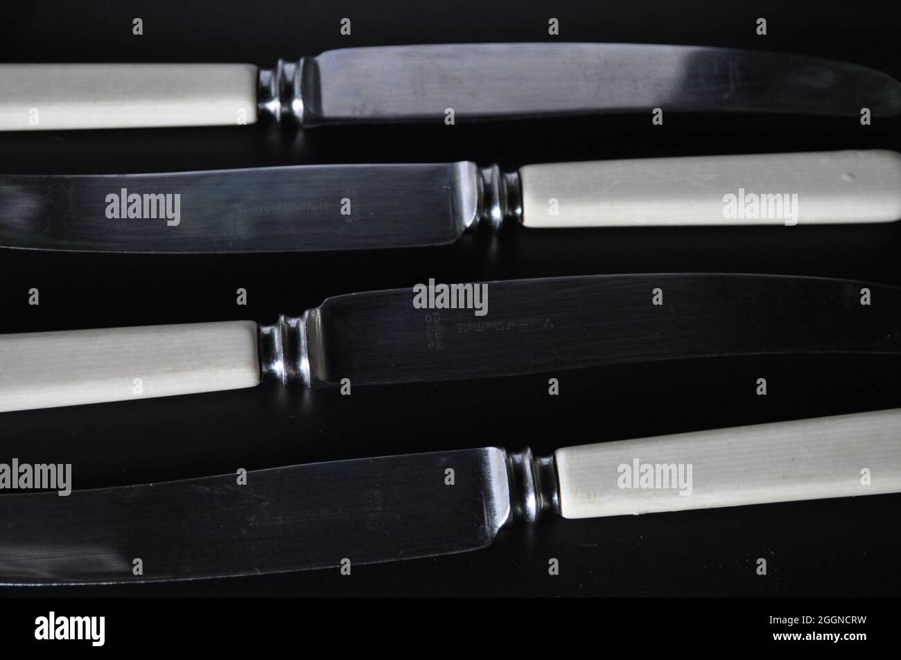 Antique butter knives set against a black background in a repeating ...