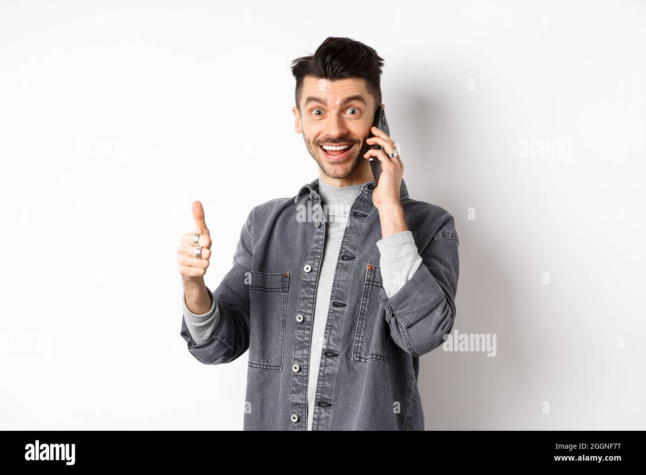 Excited young man talking on phone and showing thumbs up, smiling ...