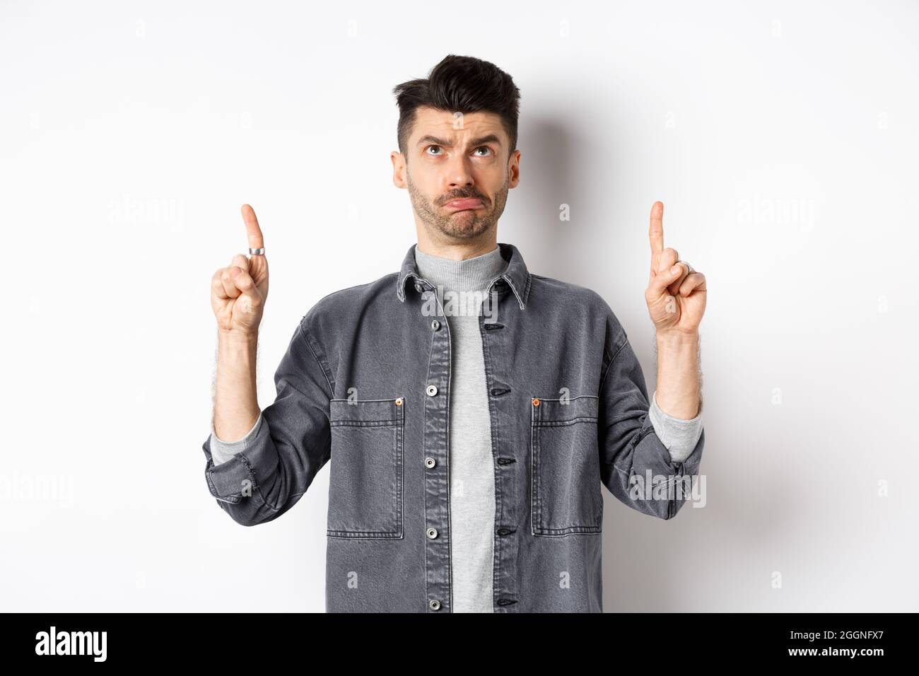 Sad frowning guy pointing and looking up, standing hesitant on white ...