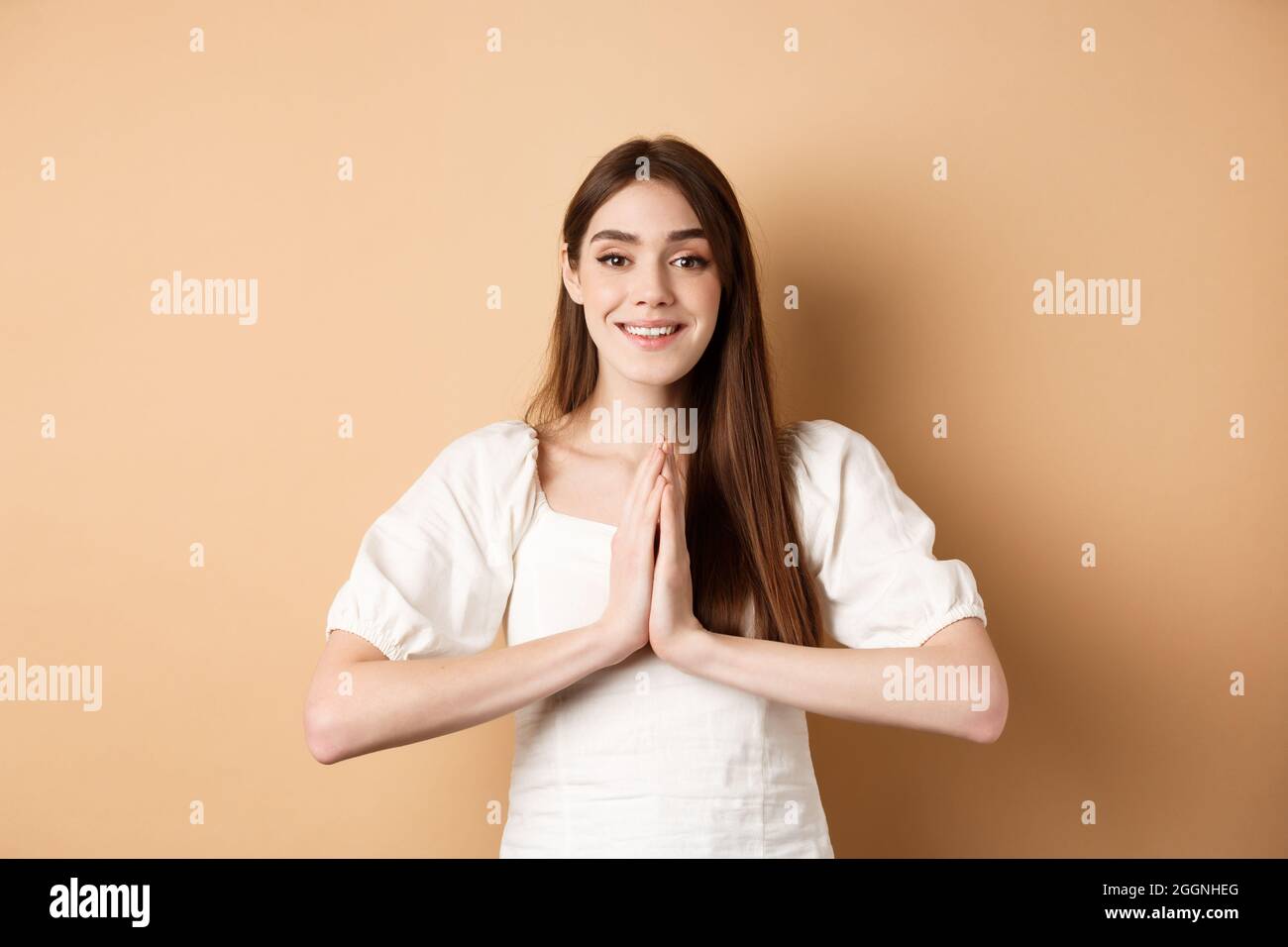 Pretty please. Cute young woman asking for favour, holding hands in ...