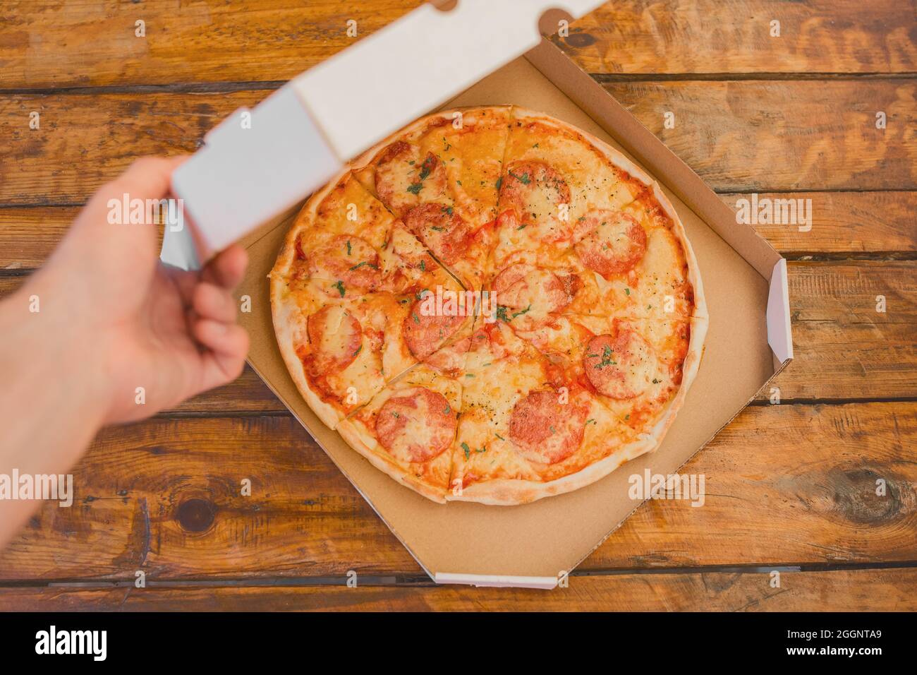 The guy's hand opens a cardboard box of pizza against the background of ...