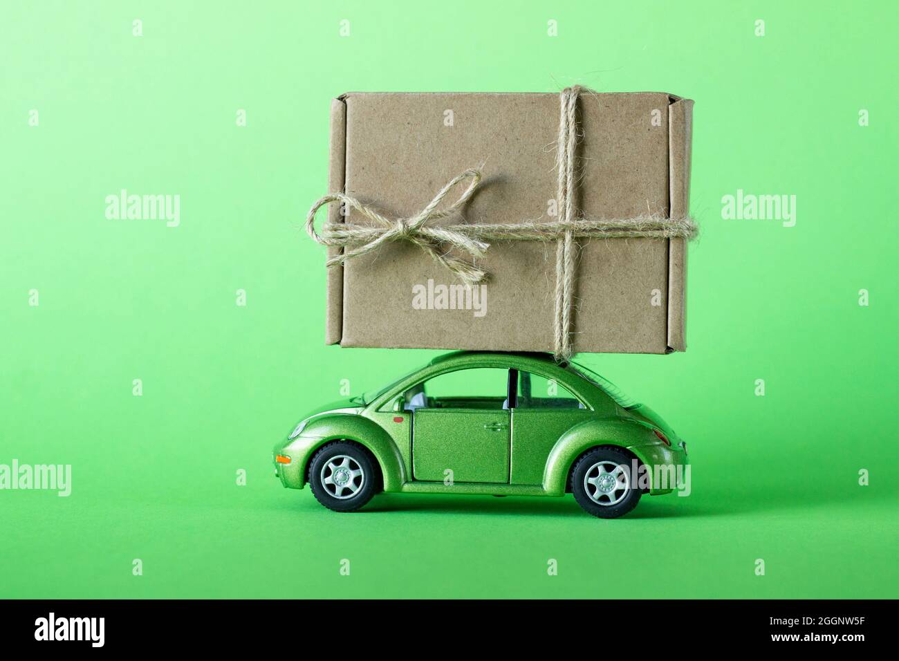 Green toy car delivers a parcel in a craft cardboard box on a pastel ...
