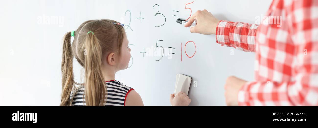 Little girl and teacher solving math equations on blackboard Stock ...