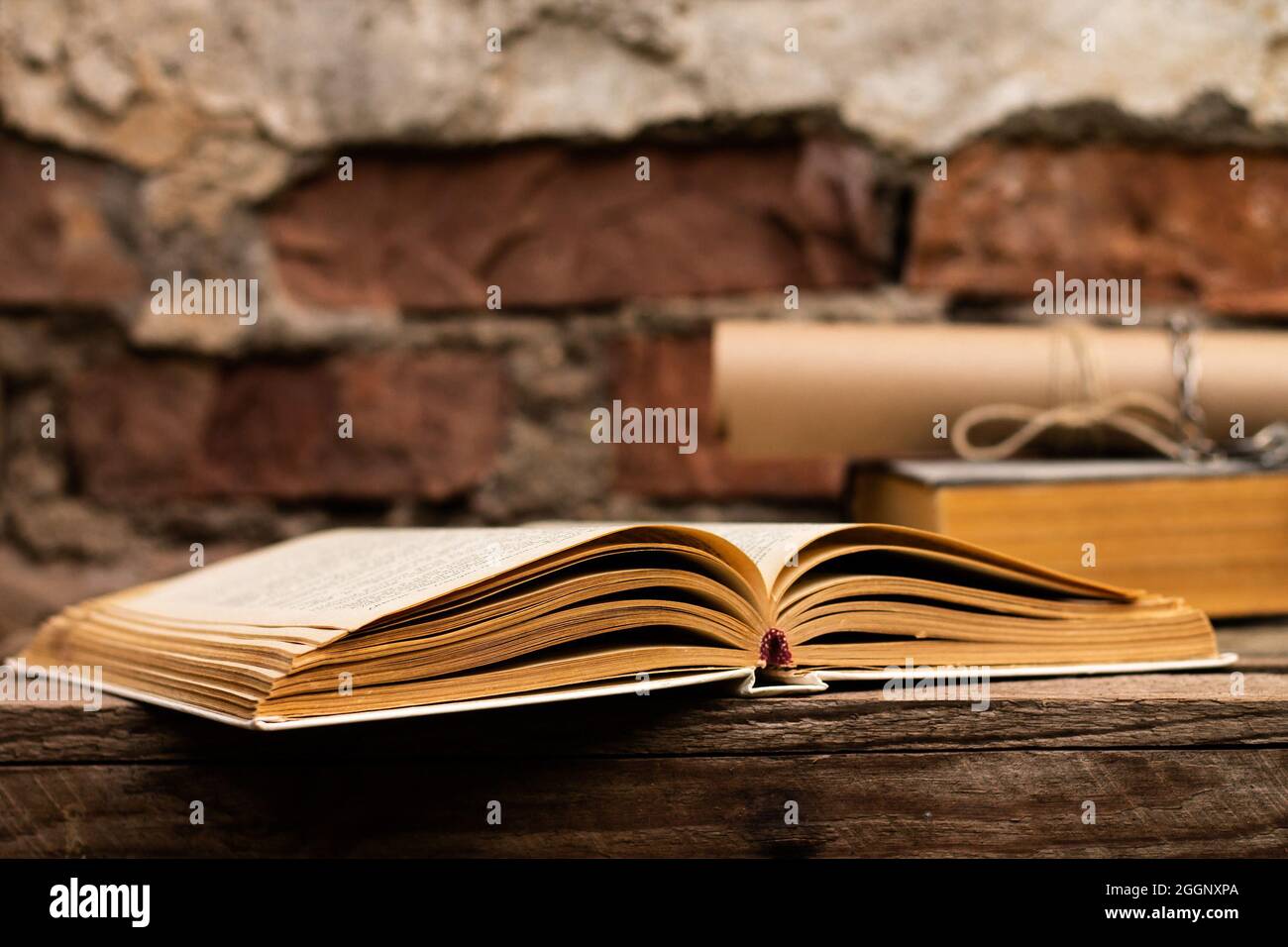 Old books with a scroll and key on a rustic wooden surface on a brick ...