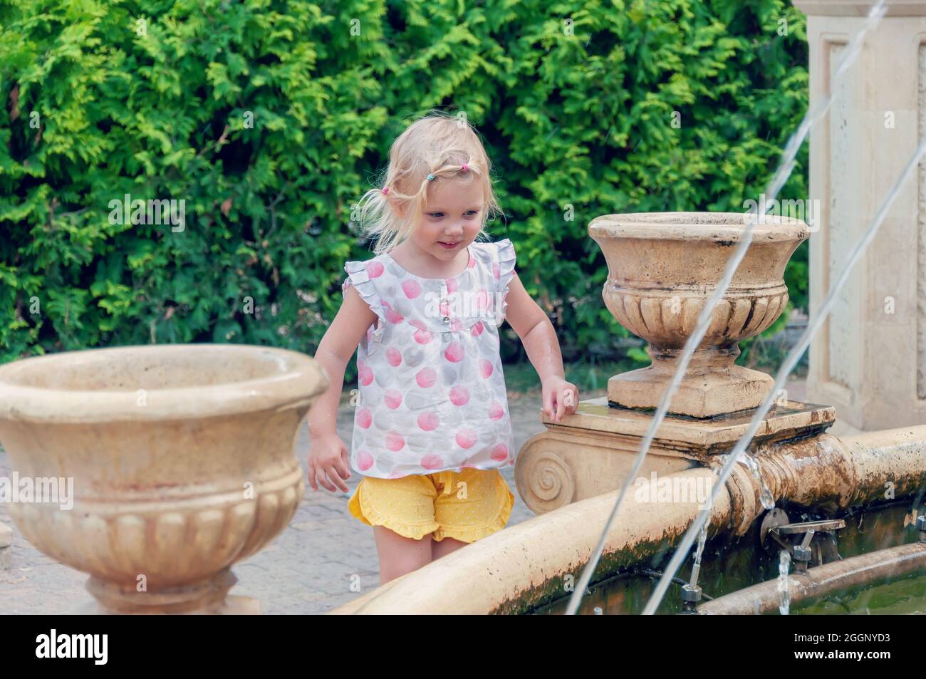 Near The Fountain. Girl having fun with fountain at hot sunny day. Cute ...