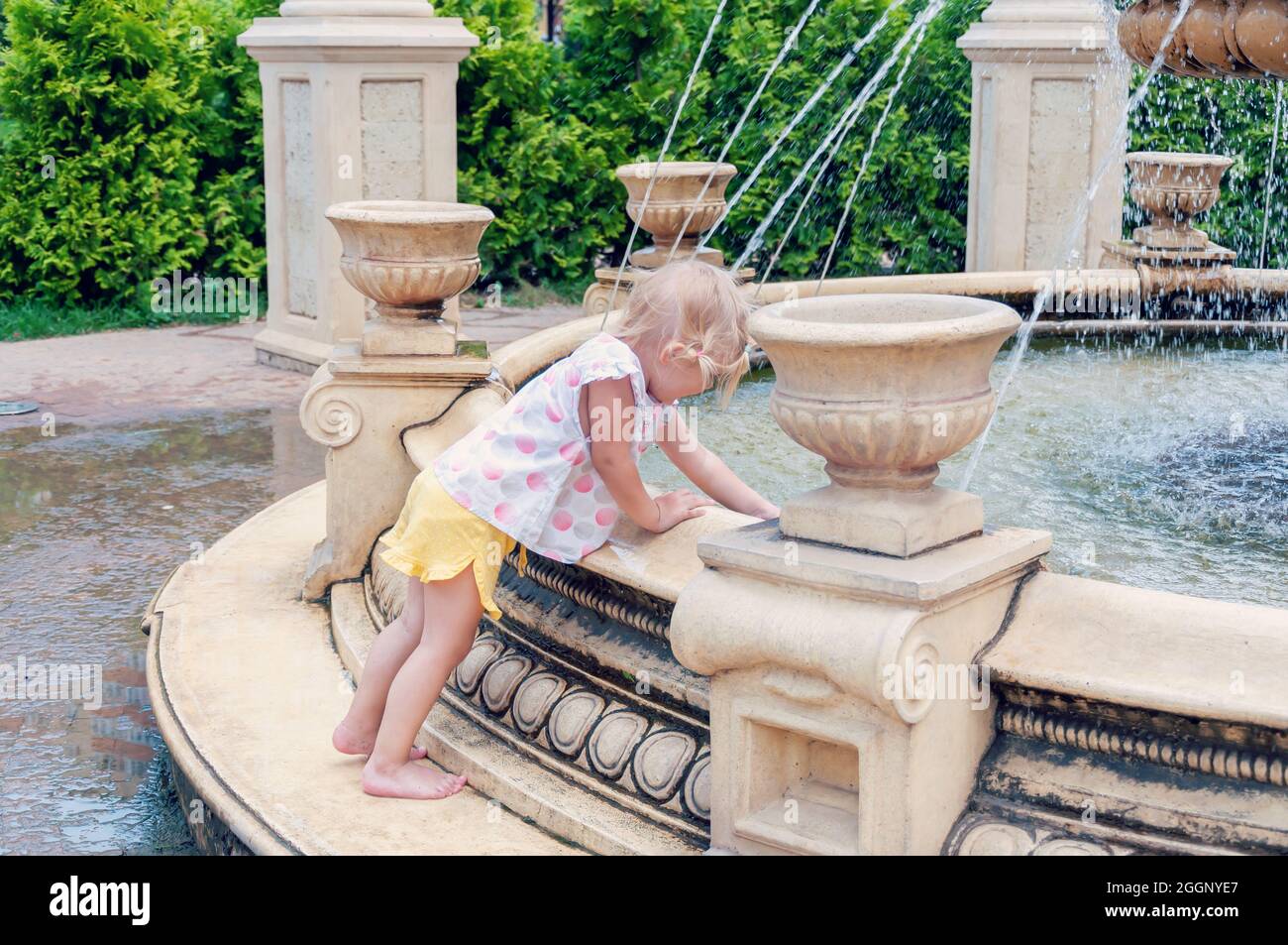 Near The Fountain. Girl having fun with fountain at hot sunny day. Cute ...