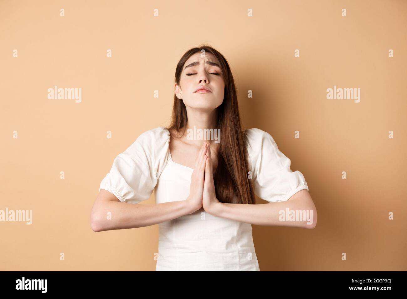 Hopeful woman close eyes and pray god, holding hands in begging gesture ...