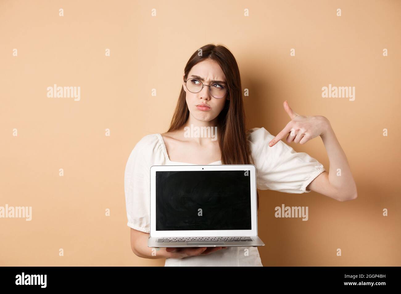 Suspicious frowning girl in glasses pointing at laptop screen, showing ...