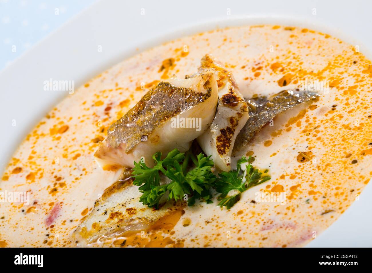 Tasty creamy soup with white fish pollock and greens at white plate ...