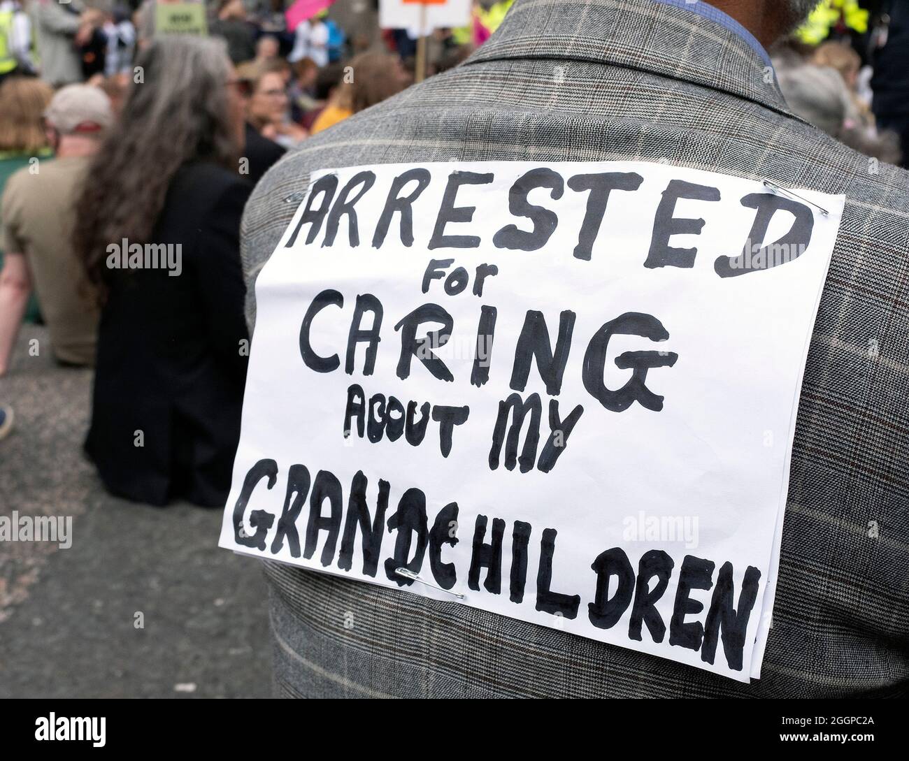 A protestor wears a placard saying 'ARRESTED FOR CARING ABOUT MY ...