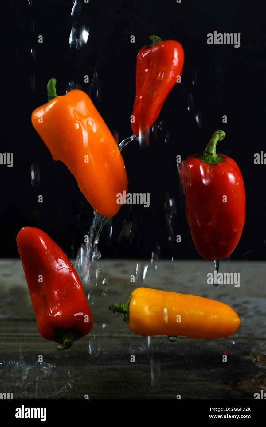 Vertical shot falling bell peppers with water on a smooth wooden ...