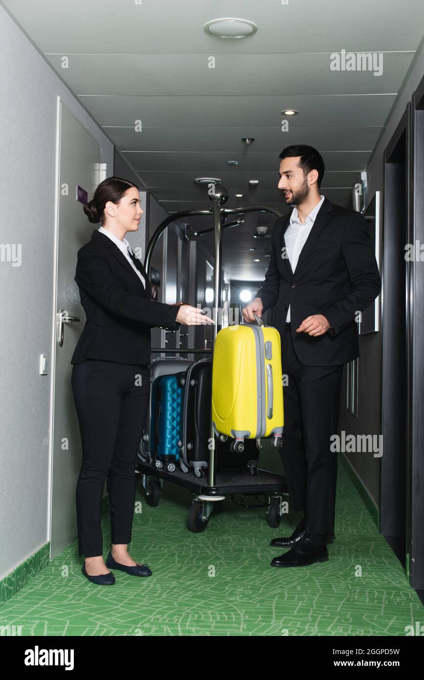 smiling receptionist pointing with hand near bellboy with luggage Stock ...