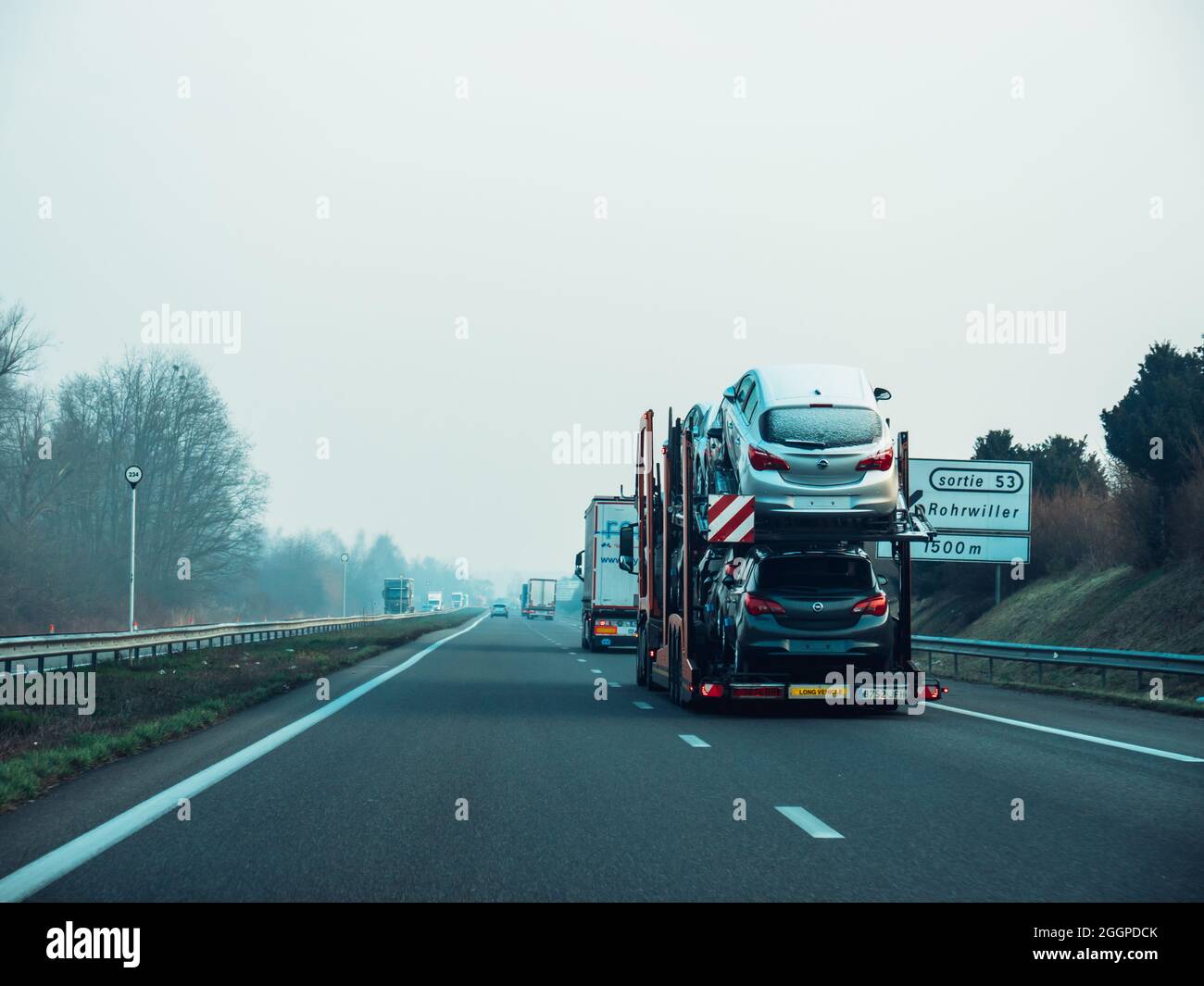 Rear view of long cargo truck carrying on the highway multiple Opel car ...