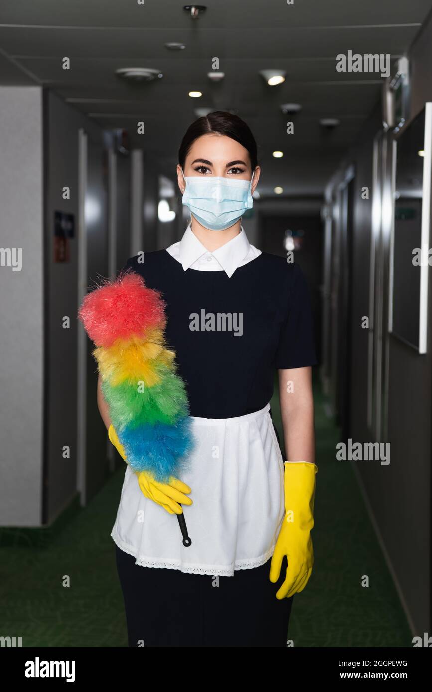 maid in medical mask and rubber gloves holding dust brush in corridor ...
