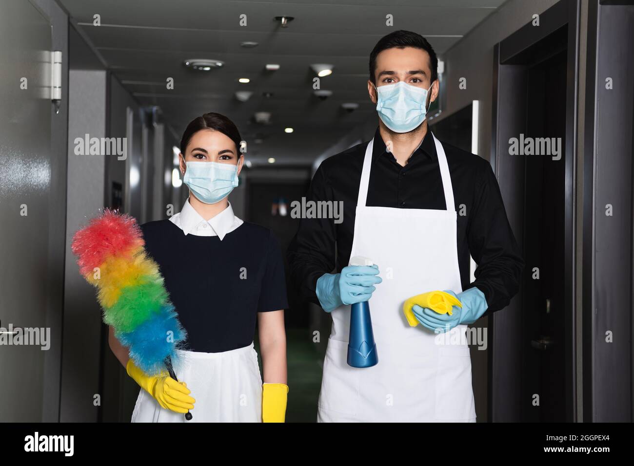 housekeepers in medical masks and rubber gloves holding spray bottle ...