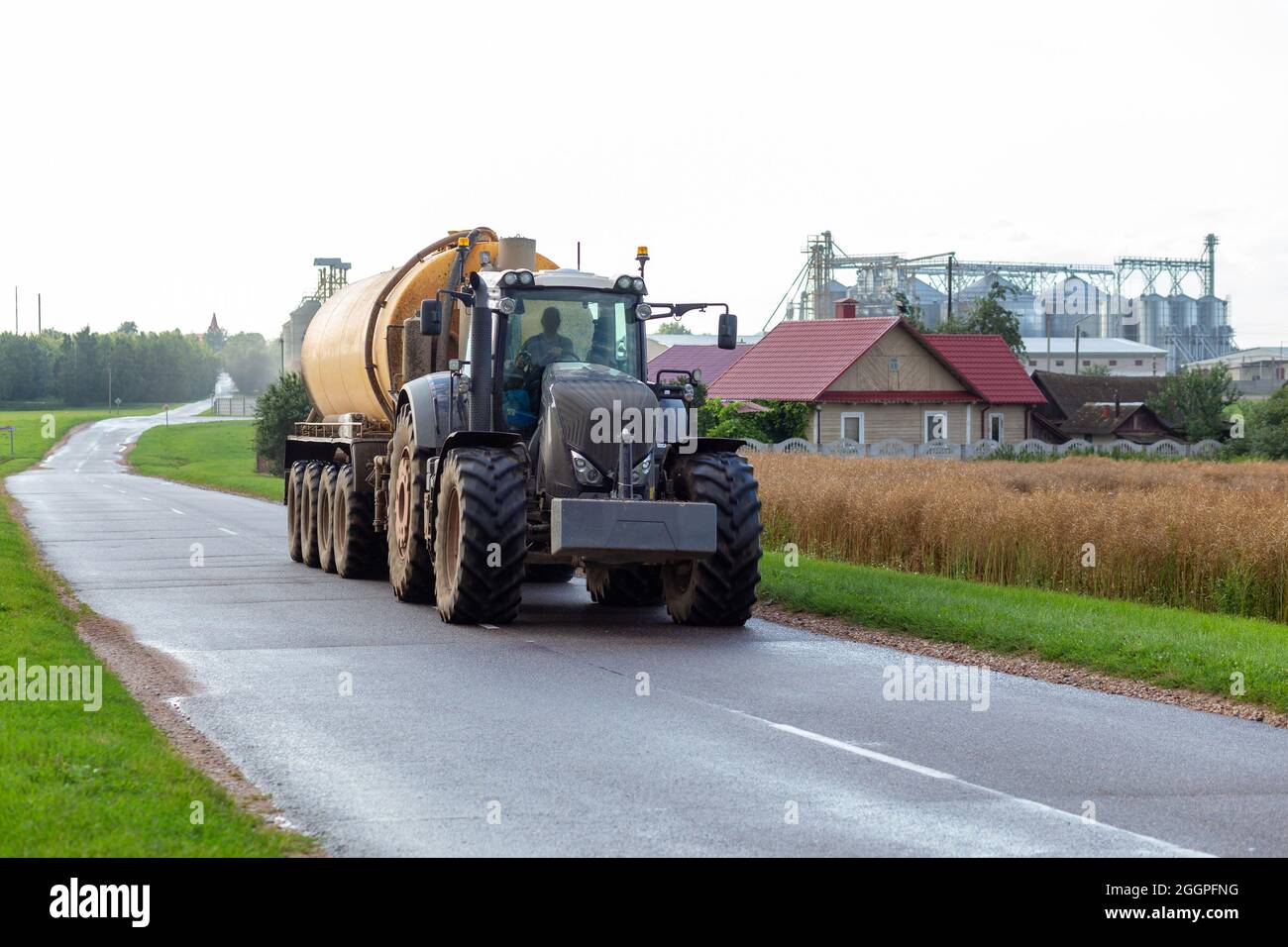 A tractor with a modern fertilizer trailer riding on the country road ...