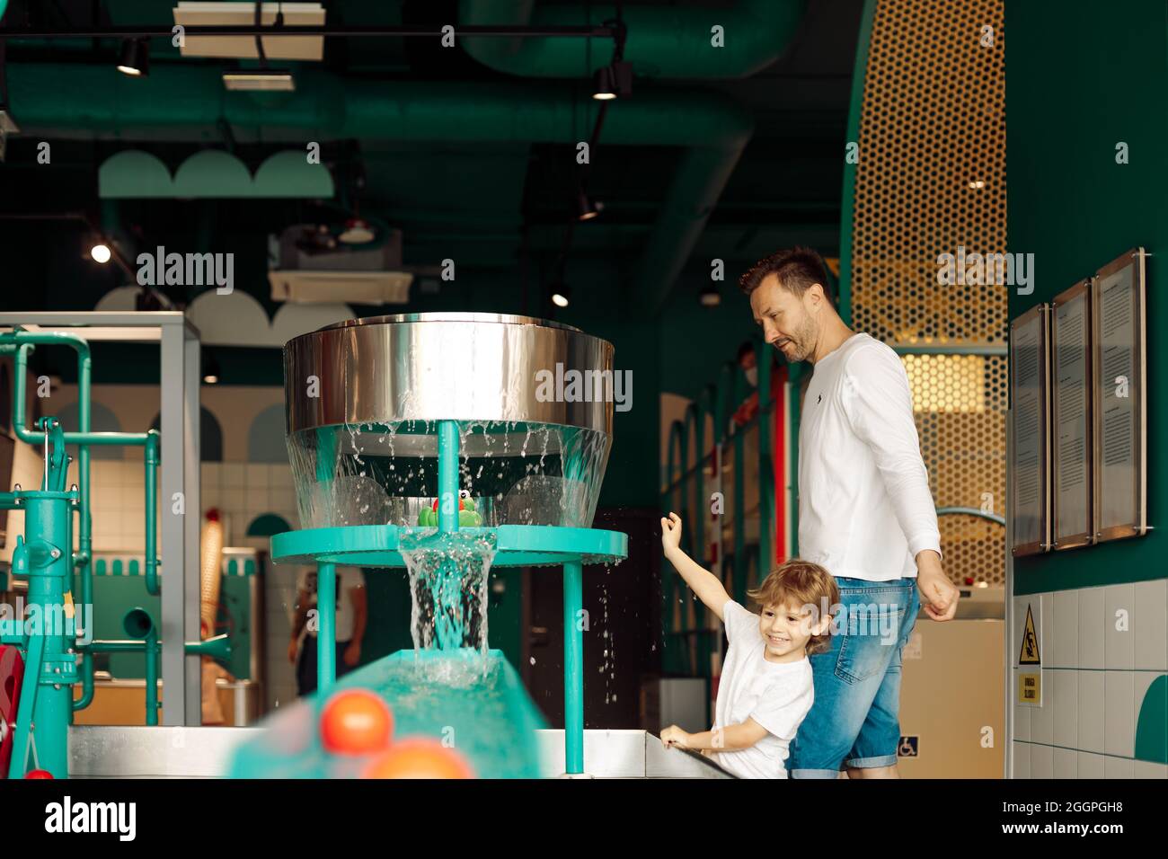 Father helps his son to play on water equipment in entertainment center ...
