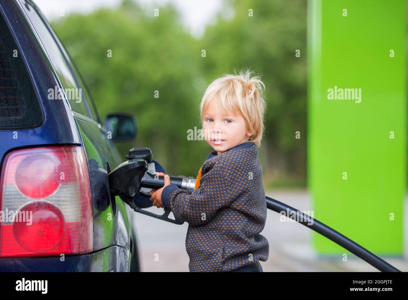Sweet little child, blond boy, helping parents to put fuel in the car ...