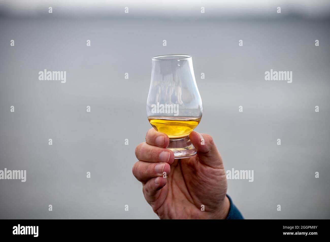 Hand holding dram of single malt scotch whisky on seashore in Scotland ...