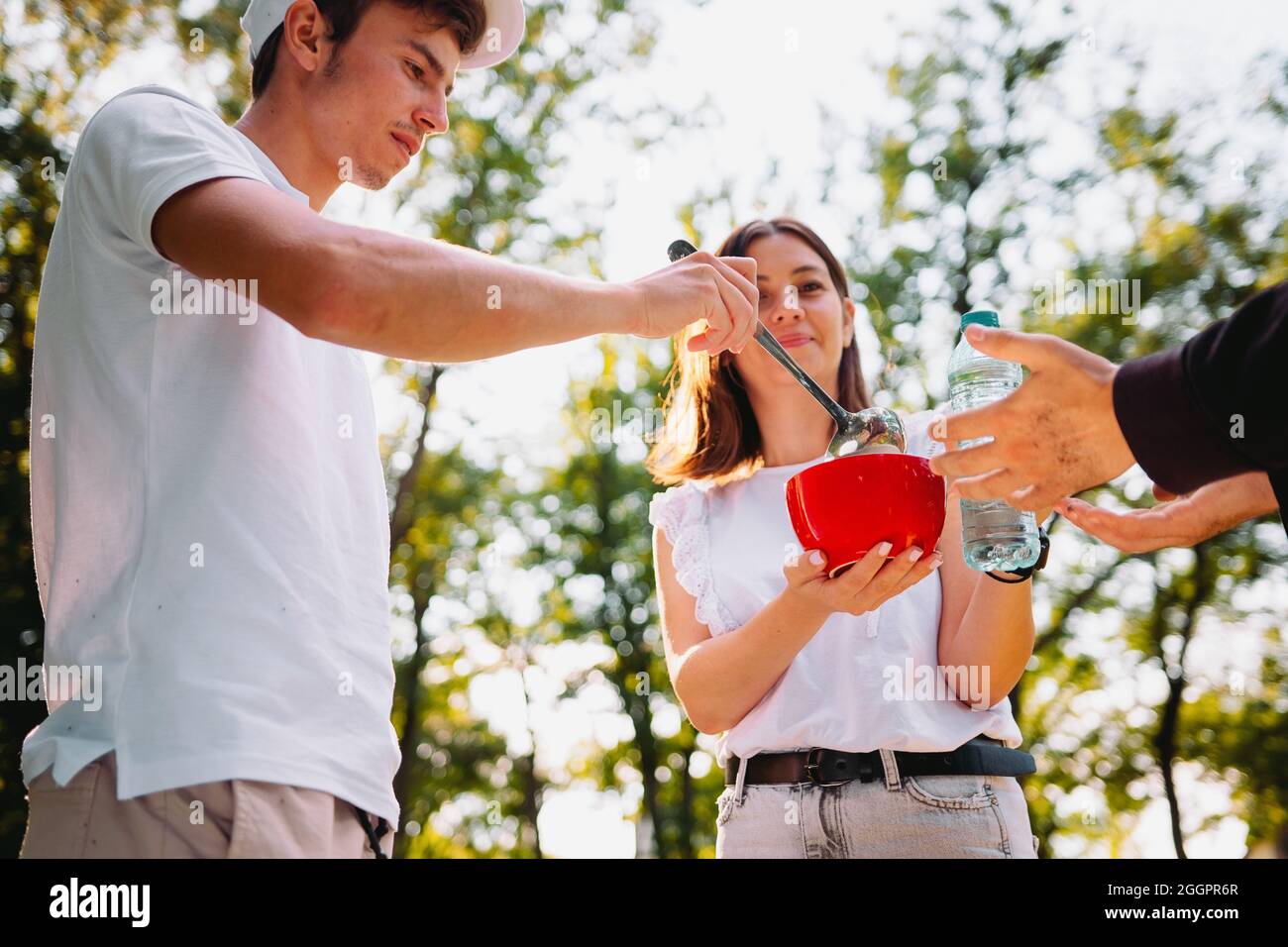 A couple of volunteer helping one homeless man giving to him a bowl of ...