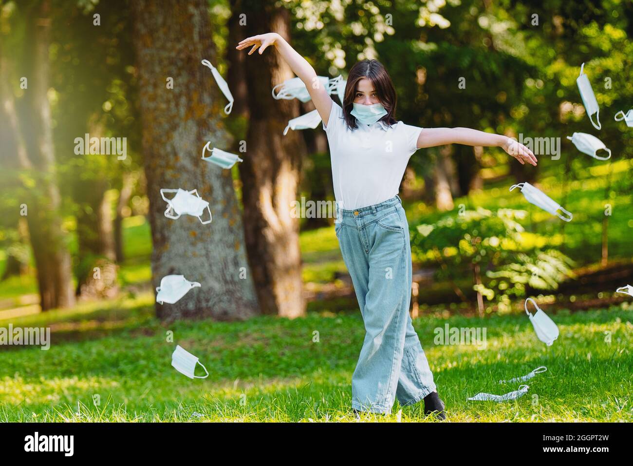 Happy young woman wearing medical mask while standing in the park in a ...