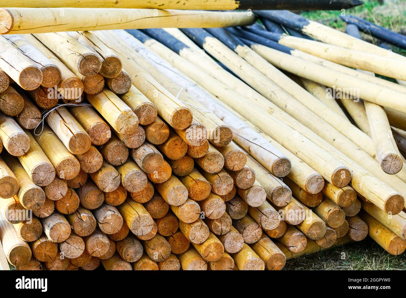 heap with long round natural wooden fence posts with tarred and ...