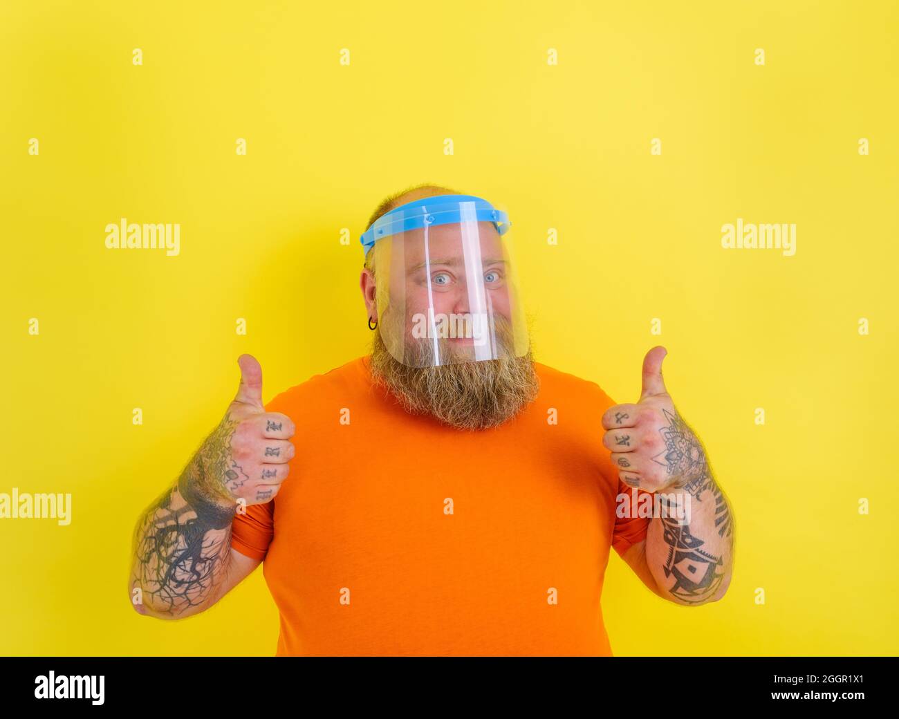 Happy man with beard and tattoos wears a protective face shield against ...
