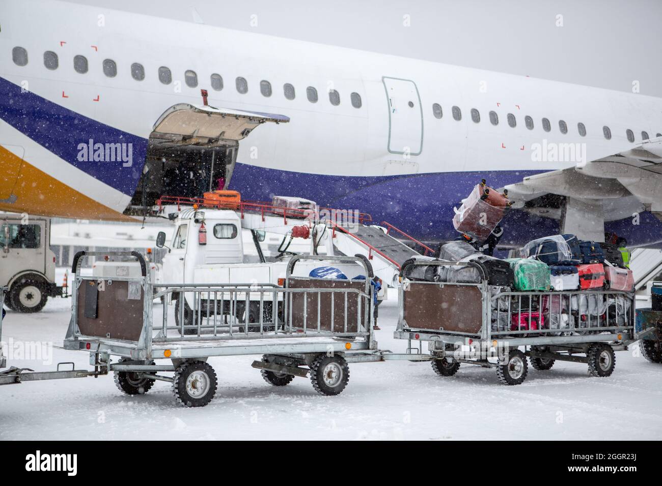 baggage loading at airport in winter. Luggage in carts near aircraft in ...