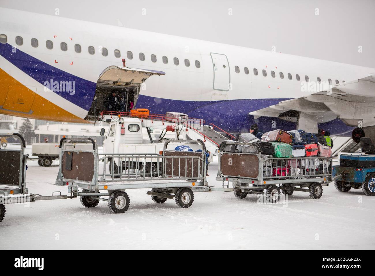 baggage loading at airport in winter. Luggage in carts near aircraft in ...