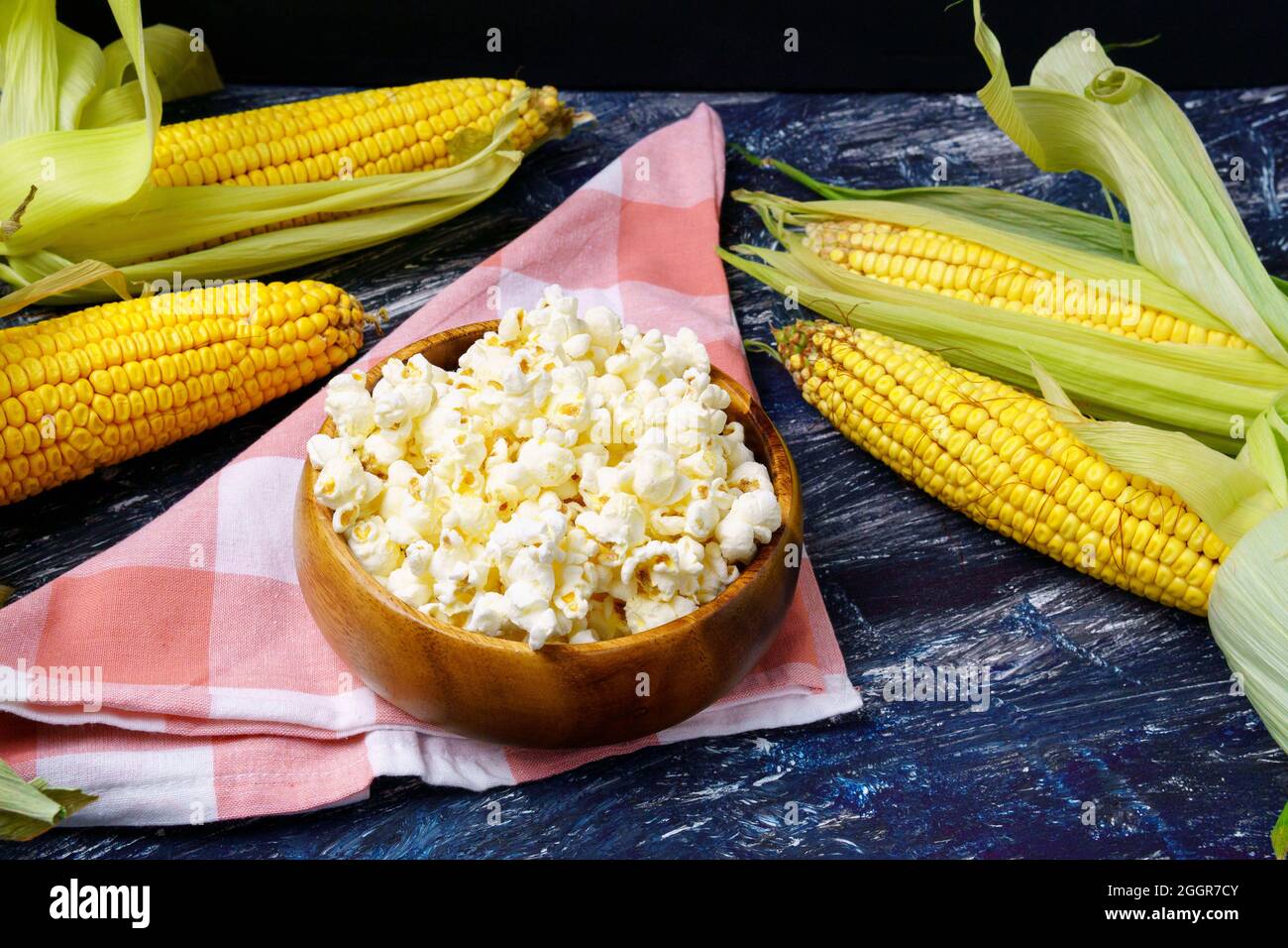 Tasty popcorn in a bowl on the table. Ears of fresh corn on a dark ...