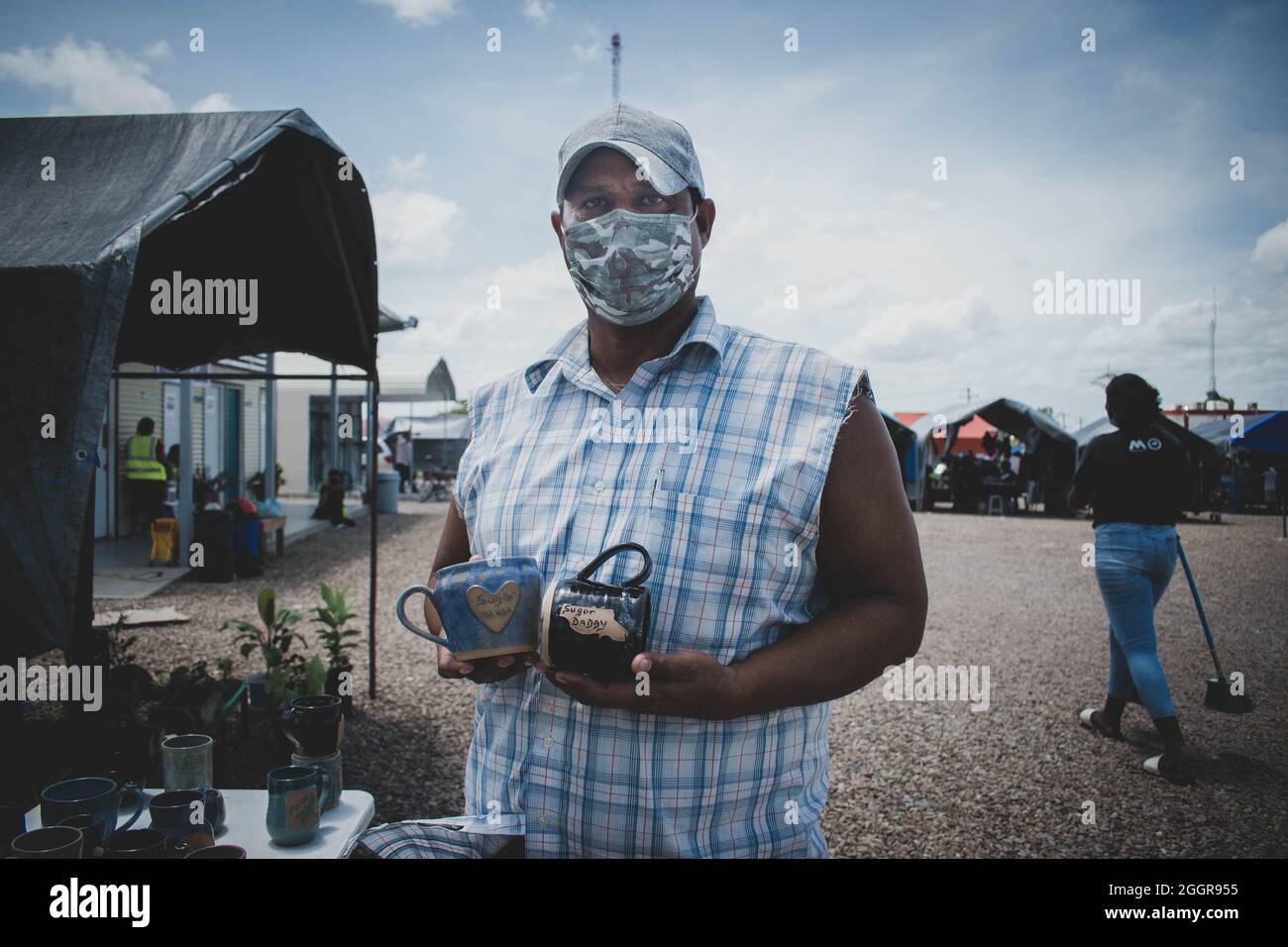 A vendor with a mask on selling household items on market day. Belmopan ...