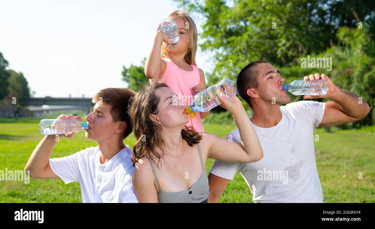 Parents with teenager son and daughter drinking cold water from plastic ...