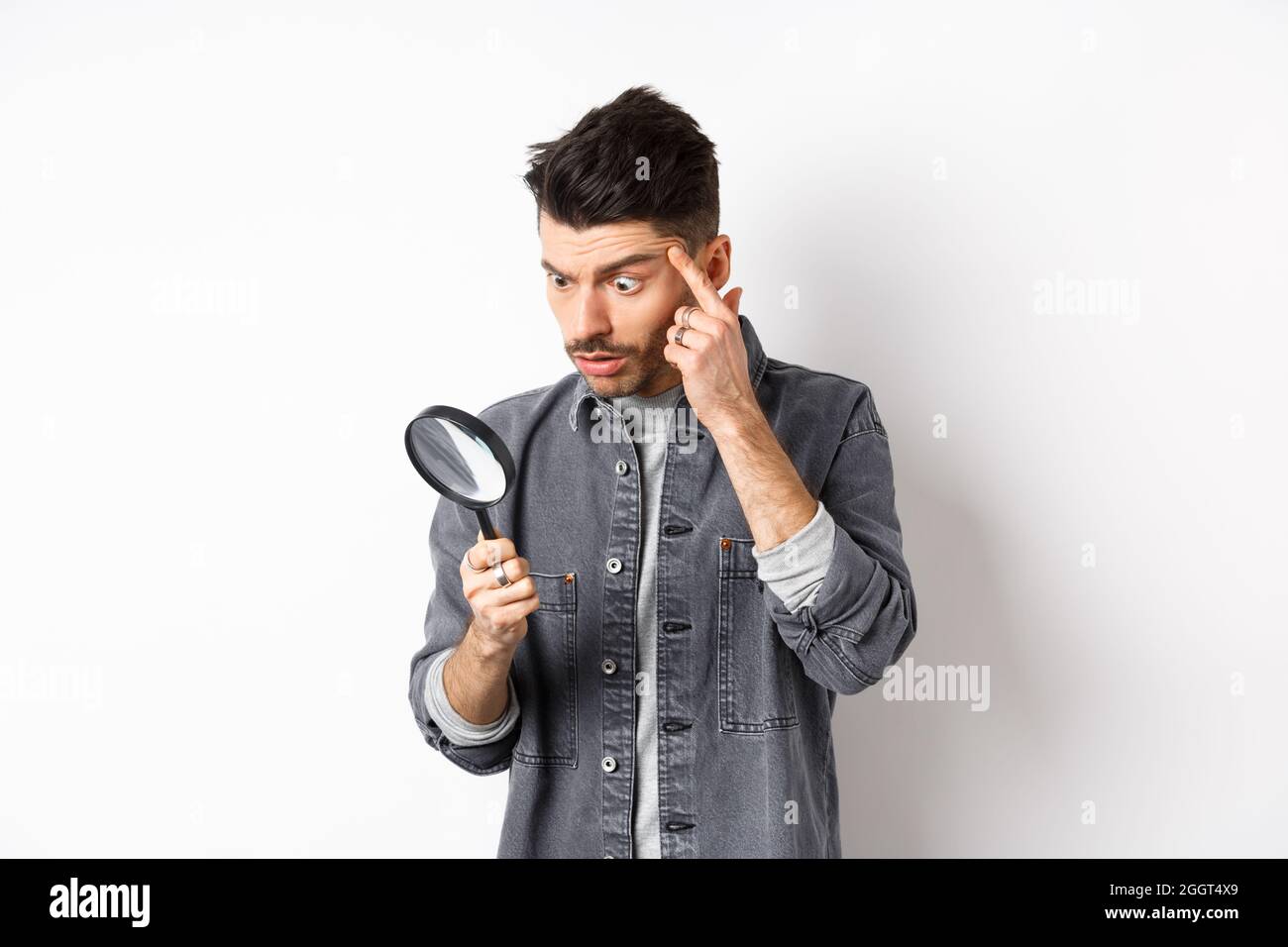 Man looking through magnifying glass and stretching eyelid to see ...