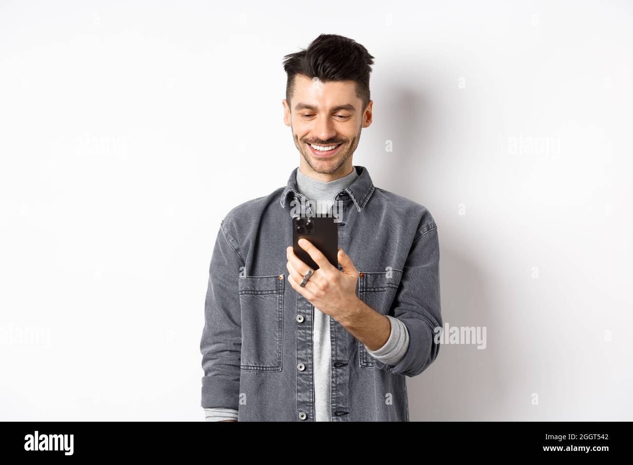 Handsome man reading message on phone and smiling. Guy holding ...