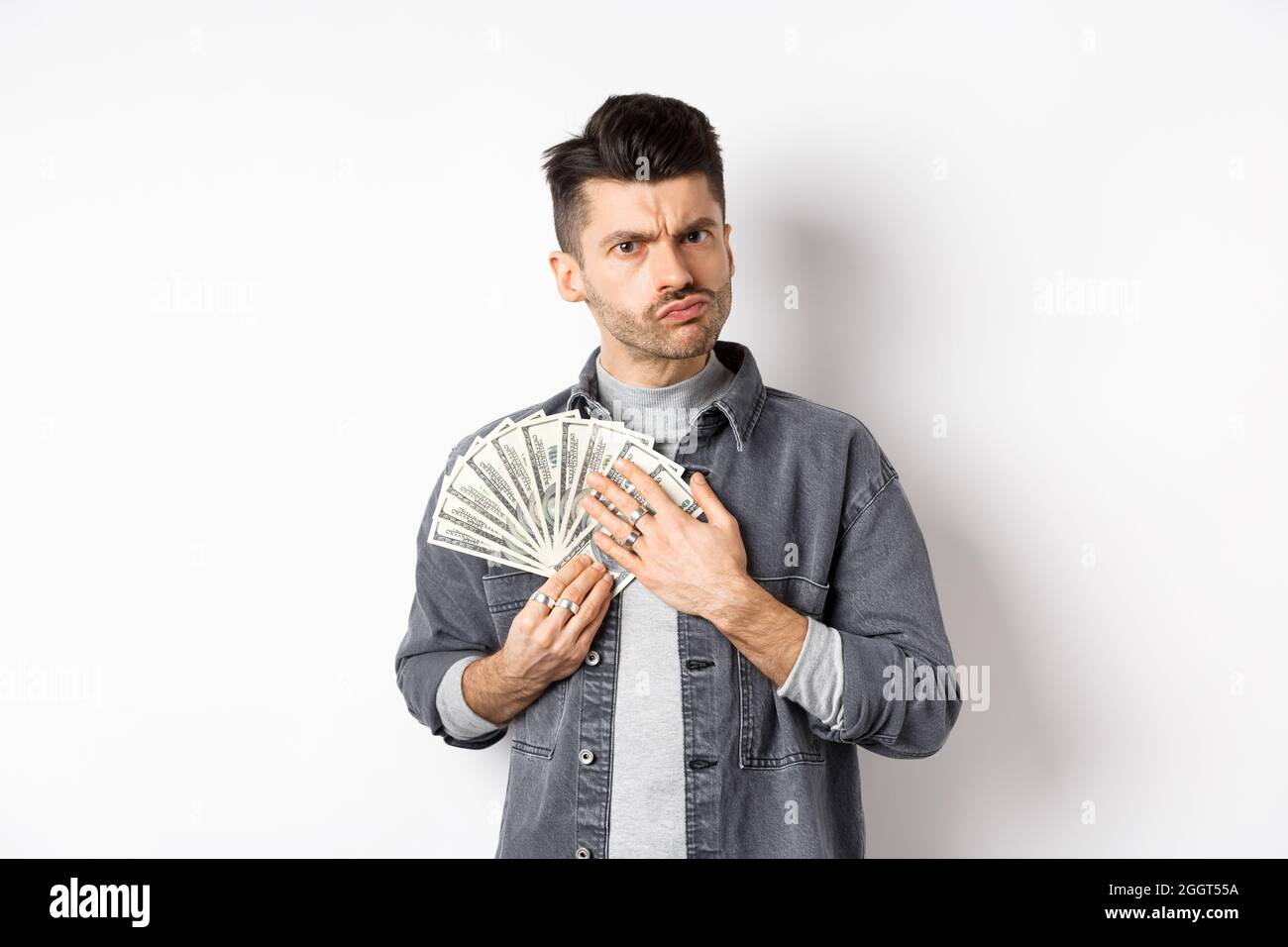 Greedy guy frowning and hugging dollar bills, unwilling to share money ...